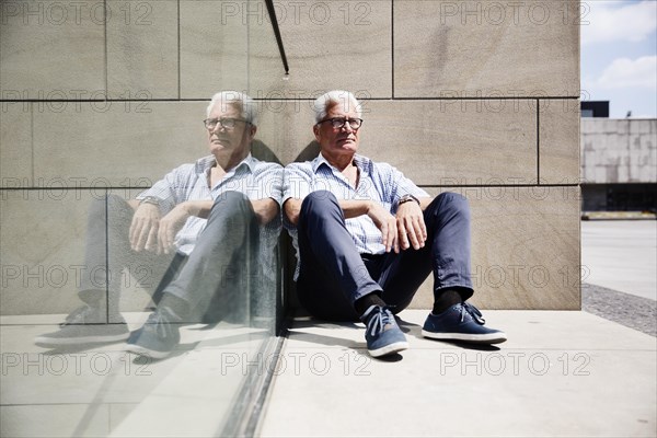 Grey-haired senior on the floor in front of a wall and reflected in a ...