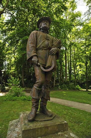 Sculpture of a spelt farmer holding a sickle and a bundle of grain ...