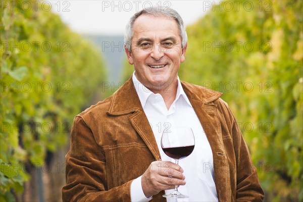 Winemaker or vintner standing with a glass of red wine in his vineyard ...