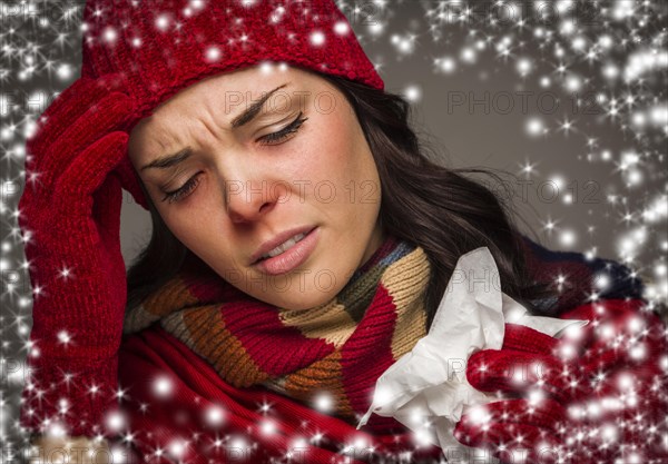 Sick mixed-race woman wearing winter hat and gloves with a tissue and ...