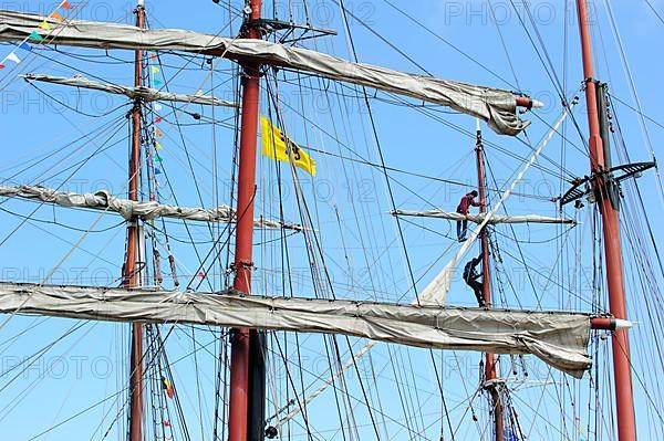 Two sailors climb the rigging to reach the yard of a sailing ship ...