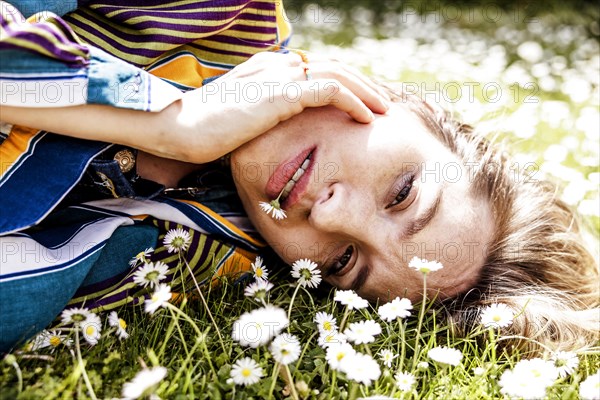 Pretty young woman lying in the grass between daisies with a daisy in ...