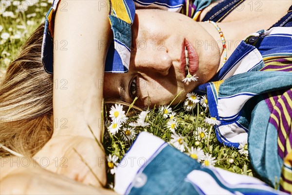 Pretty young woman lying in the grass between daisies with a daisy in ...