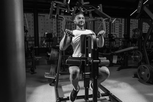 Handsome young man pumps his shoulders in a special machine. Fitness ...