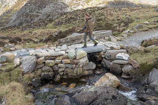 Woman walking over stone bridge, LLyn Idwal footpath, Snowdonia ...