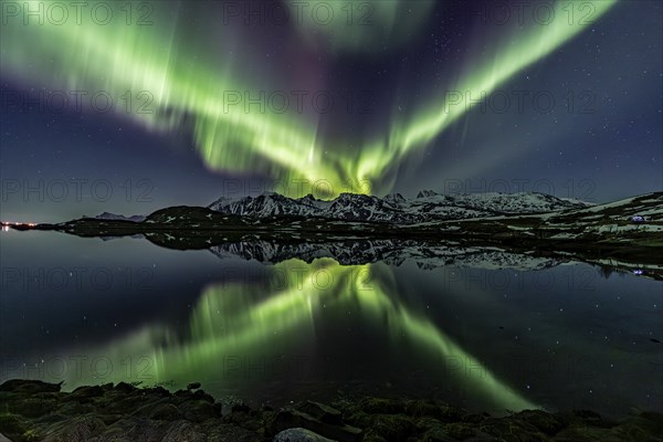Yellow and green northern lights reflected in fjord, steep mountains ...